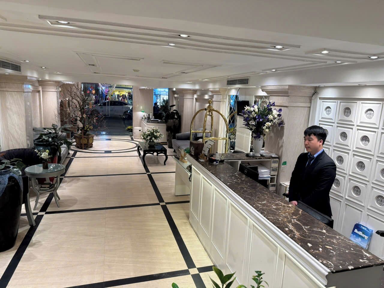 Um hall de hotel com balcão de recepção, área de estar e plantas decorativas.