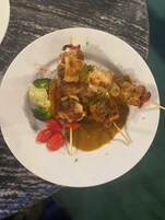 Um prato de espetinhos de carne com legumes e molho.