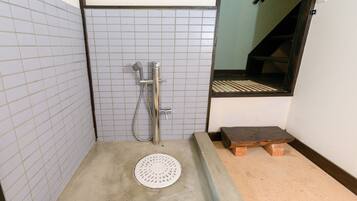 Um banheiro pequeno com azulejos, chuveiro, ralo e um banco de madeira.