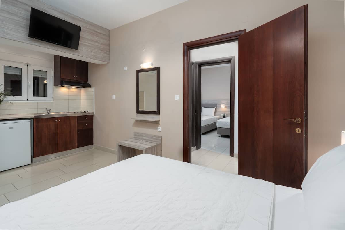 Quarto de hotel moderno com cama, mesa de cabeceira pequena, televisão integrada, espelho e vista para o quarto vizinho.