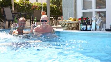 Uma piscina com duas pessoas, uma cesta de vime com frutas e garrafas de cerveja na beira da piscina.