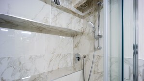 Uma casa de banho moderna com azulejos de mármore, cabine de duche de vidro e chuveiro manual.