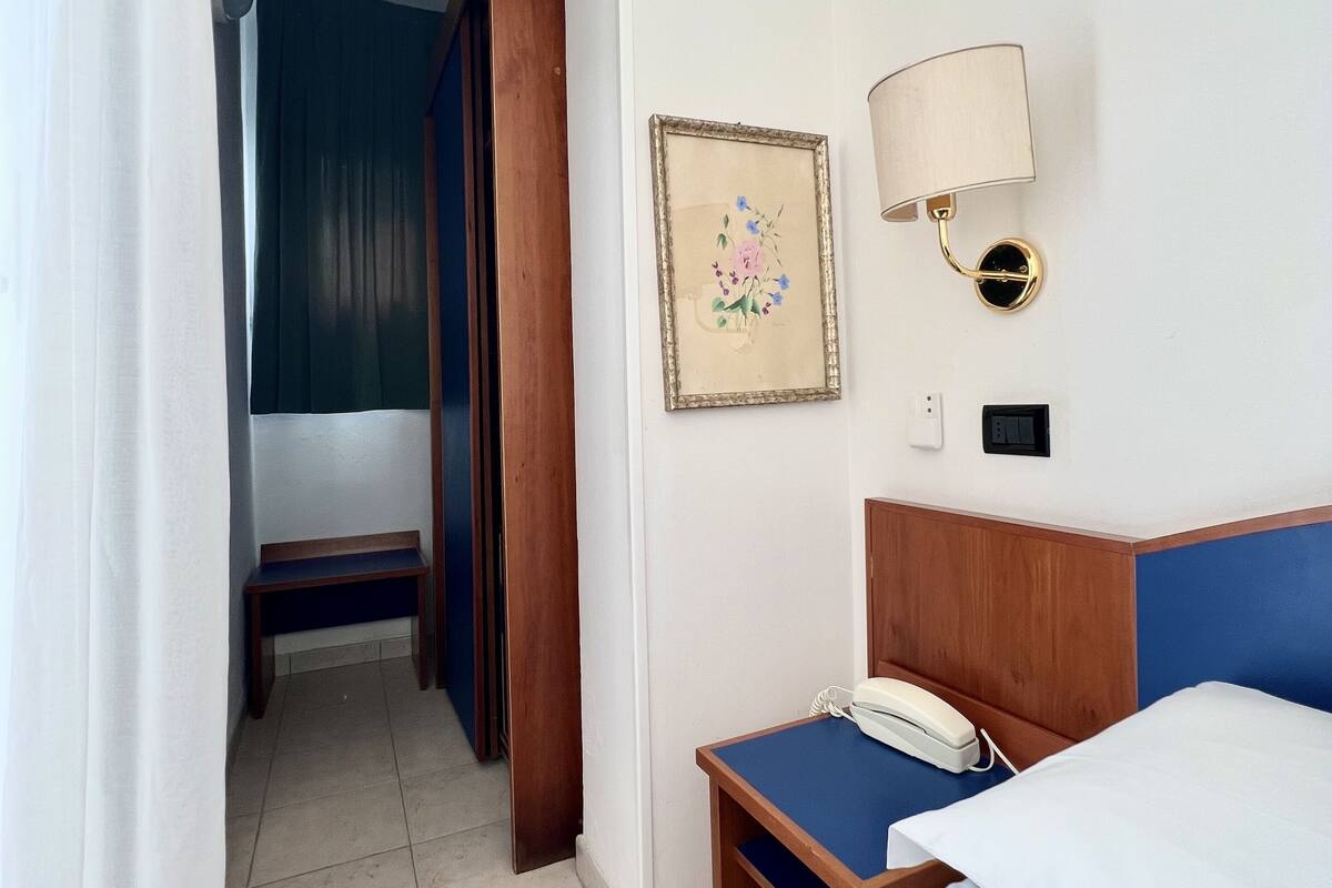 Quarto de hotel com cama, mesa de cabeceira, abajur e um quadro na parede.