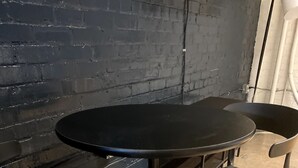 Uma mesa redonda com quatro cadeiras pretas, posicionada diante de uma parede de tijolos escuros.