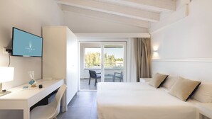 Quarto de hotel com cama, escrivaninha, cadeira, televisão e varanda vista para árvores.
