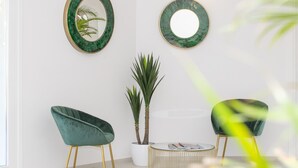 Quarto moderno com duas poltronas estofadas em verde, uma mesa de centro redonda e dois espelhos fixados na parede.