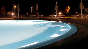 Piscina com borda iluminada, espreguiçadeiras e guarda-sóis.