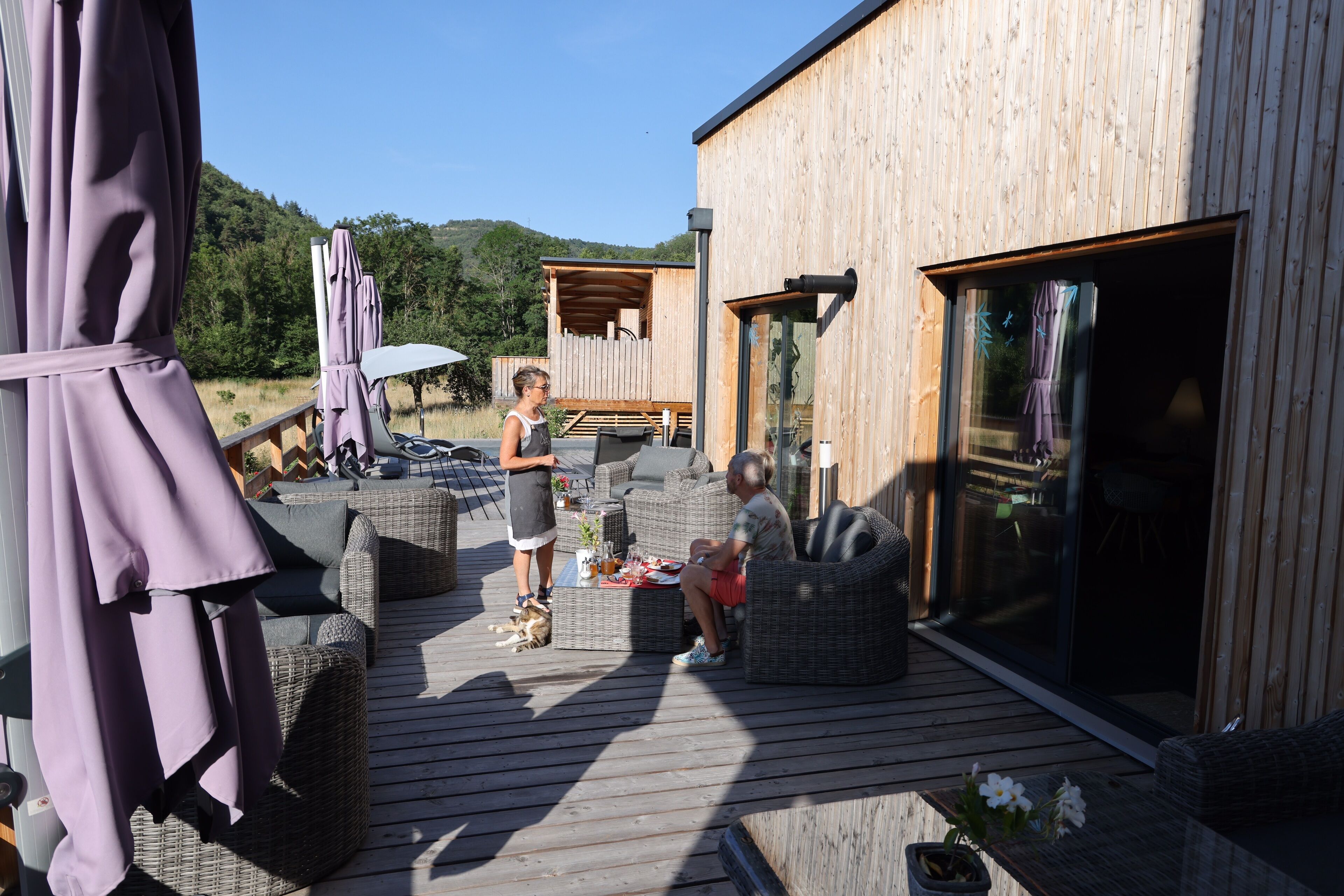 Um deck de madeira com mobiliário de exterior, uma porta de vidro e vista para a paisagem circundante.