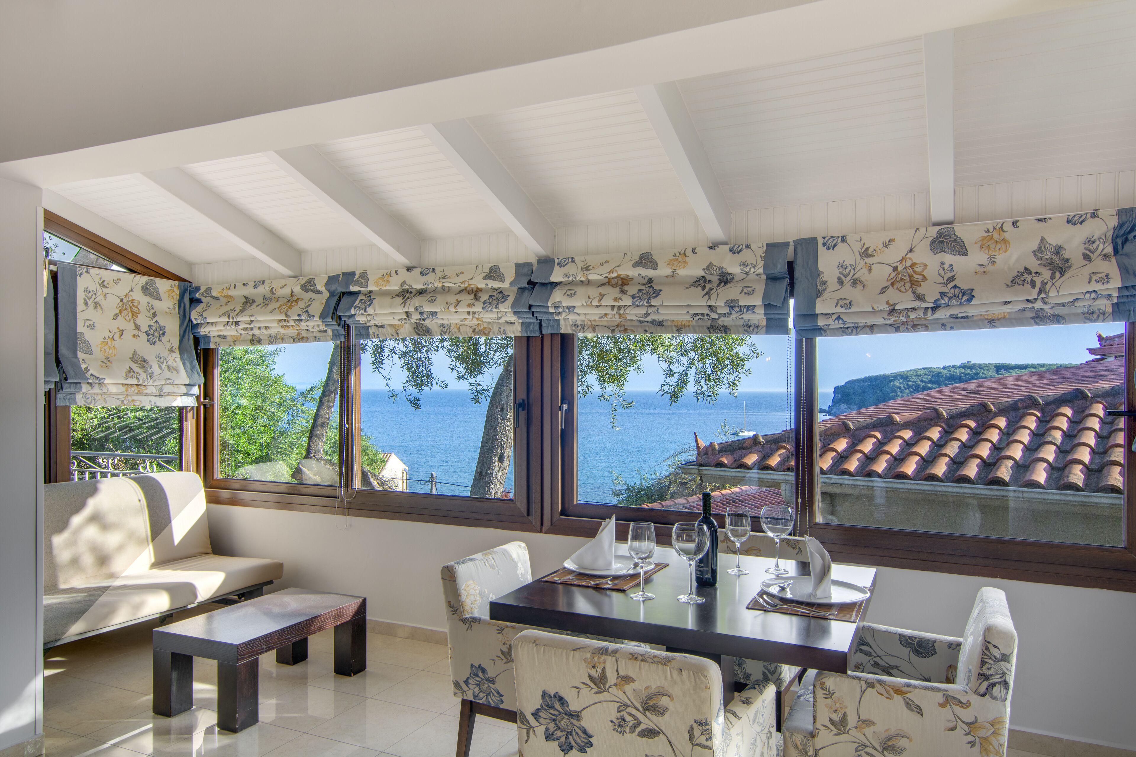 Uma sala de jantar com uma mesa posta para dois, um sofá e vista para o mar.