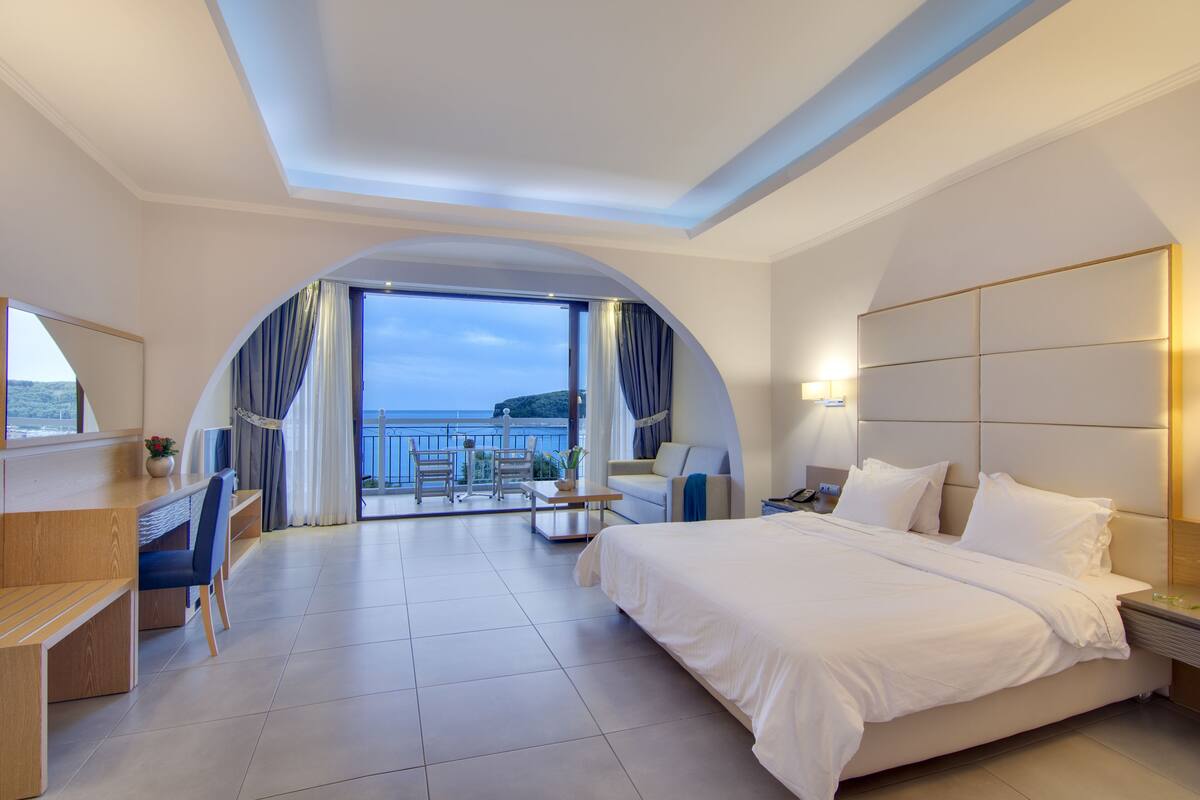 Quarto de hotel moderno com uma cama grande, uma escrivaninha e uma varanda com vista para o mar.