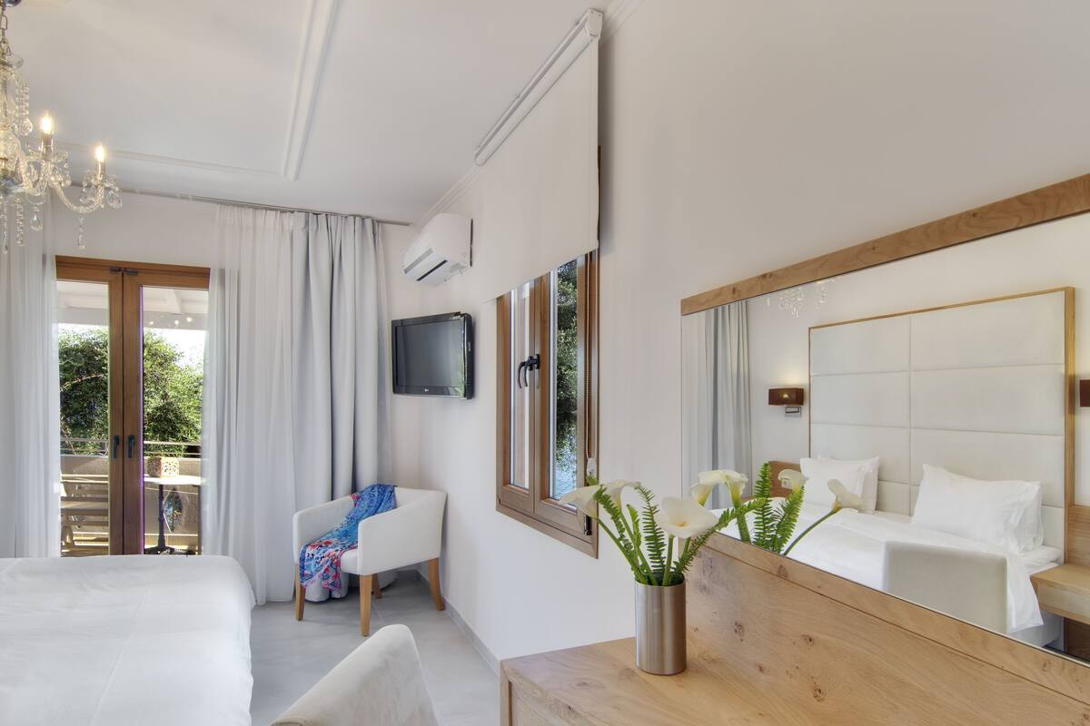 Quarto de hotel com cama, escrivaninha, cadeira, televisão e varanda com mesa e cadeiras.