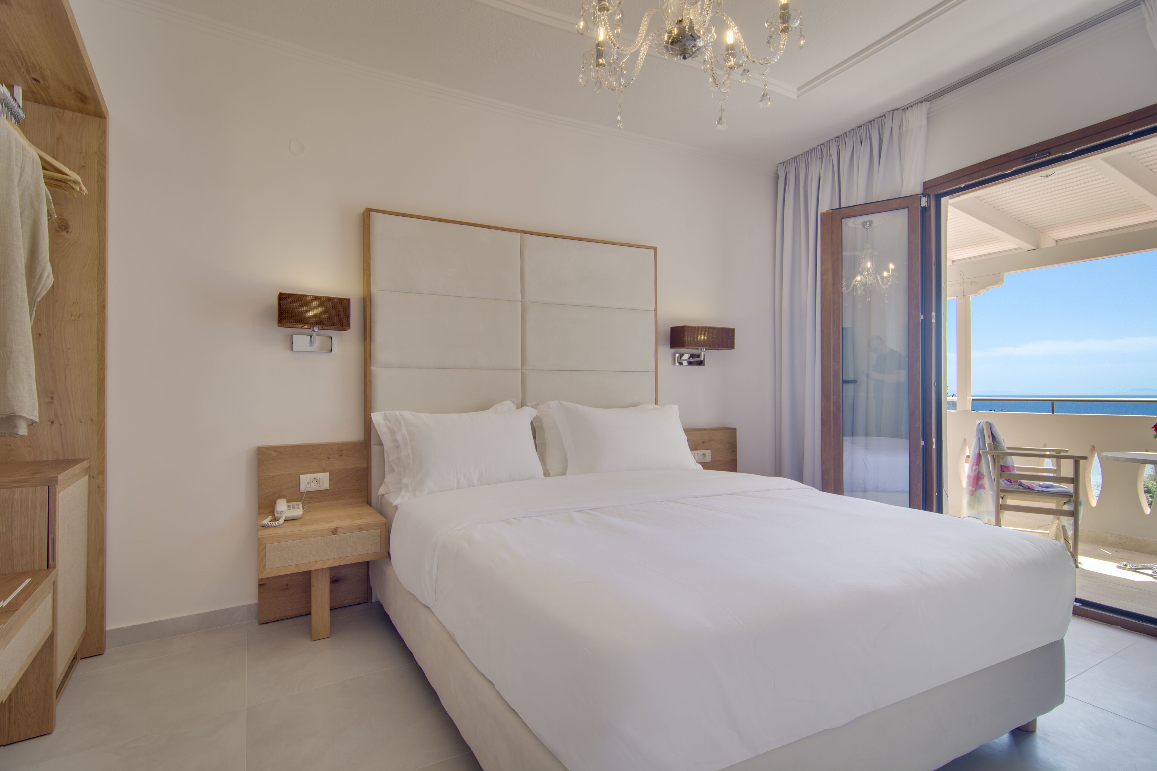 Uma cama grande com cabeceira de madeira, duas mesas de cabeceira e um lustre.