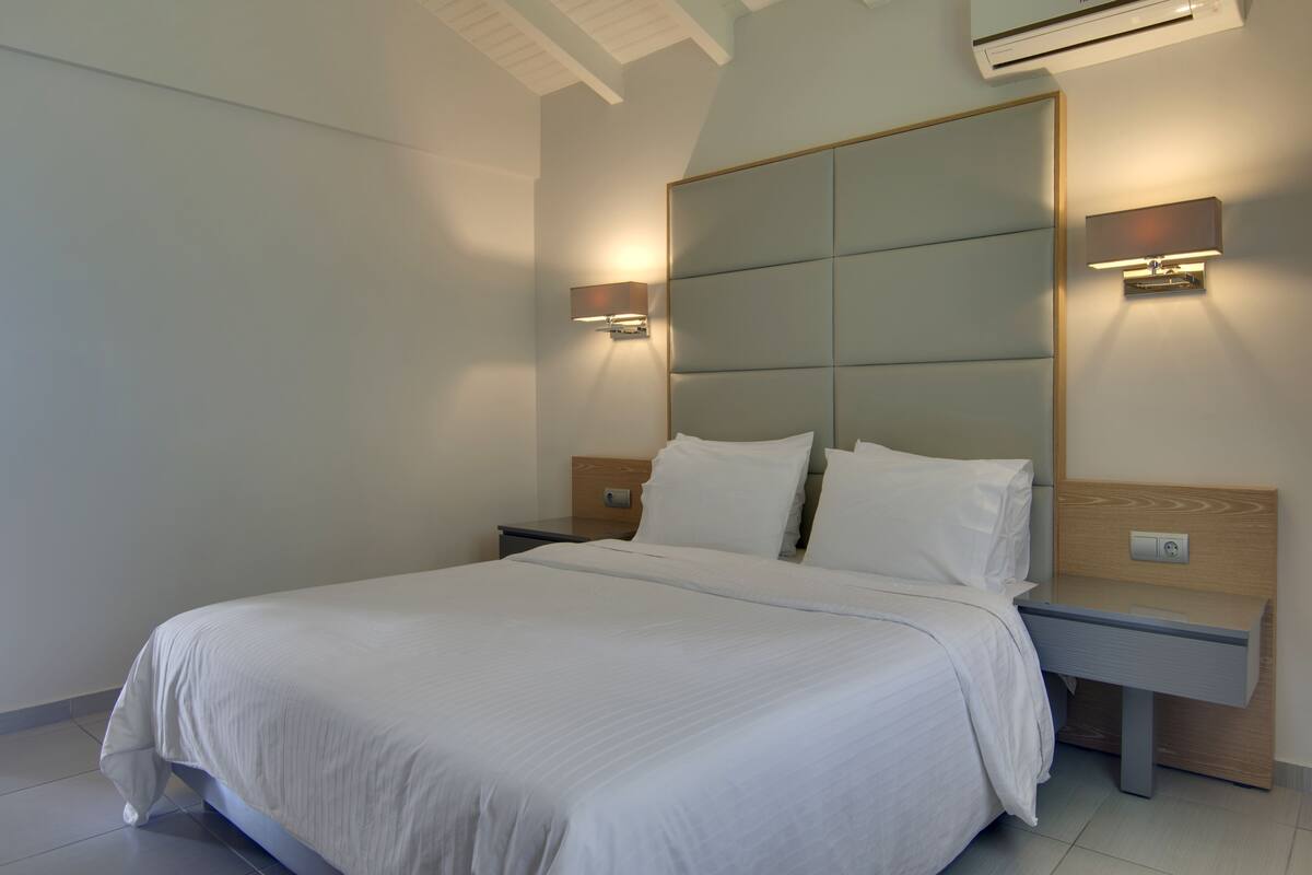Quarto de hotel moderno com uma cama grande, duas mesas de cabeceira e cabeceira com iluminação integrada.