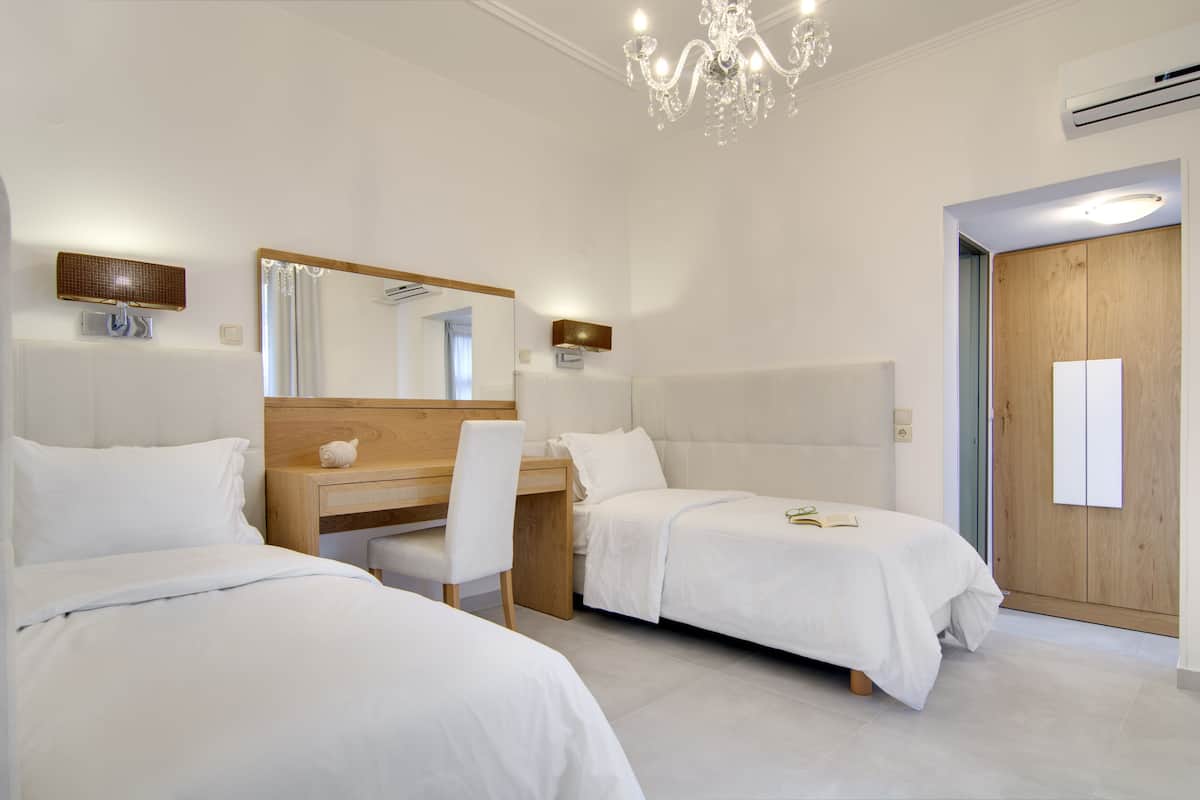 Quarto de hotel com duas camas, uma escrivaninha de madeira, uma cadeira, um espelho e um candelabro.