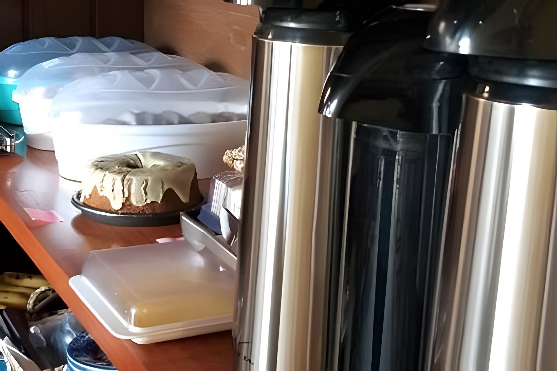 Uma bancada de cozinha com um bolo, um recipiente branco e recipientes de aço inoxidável.