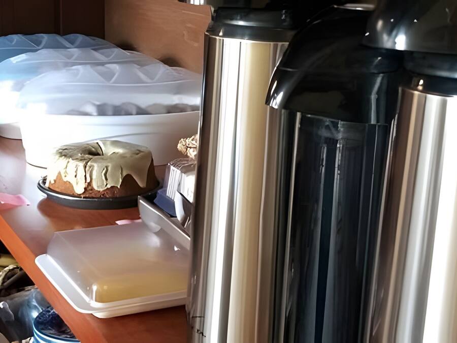 Uma bancada de cozinha com um bolo, um recipiente branco e recipientes de aço inoxidável.