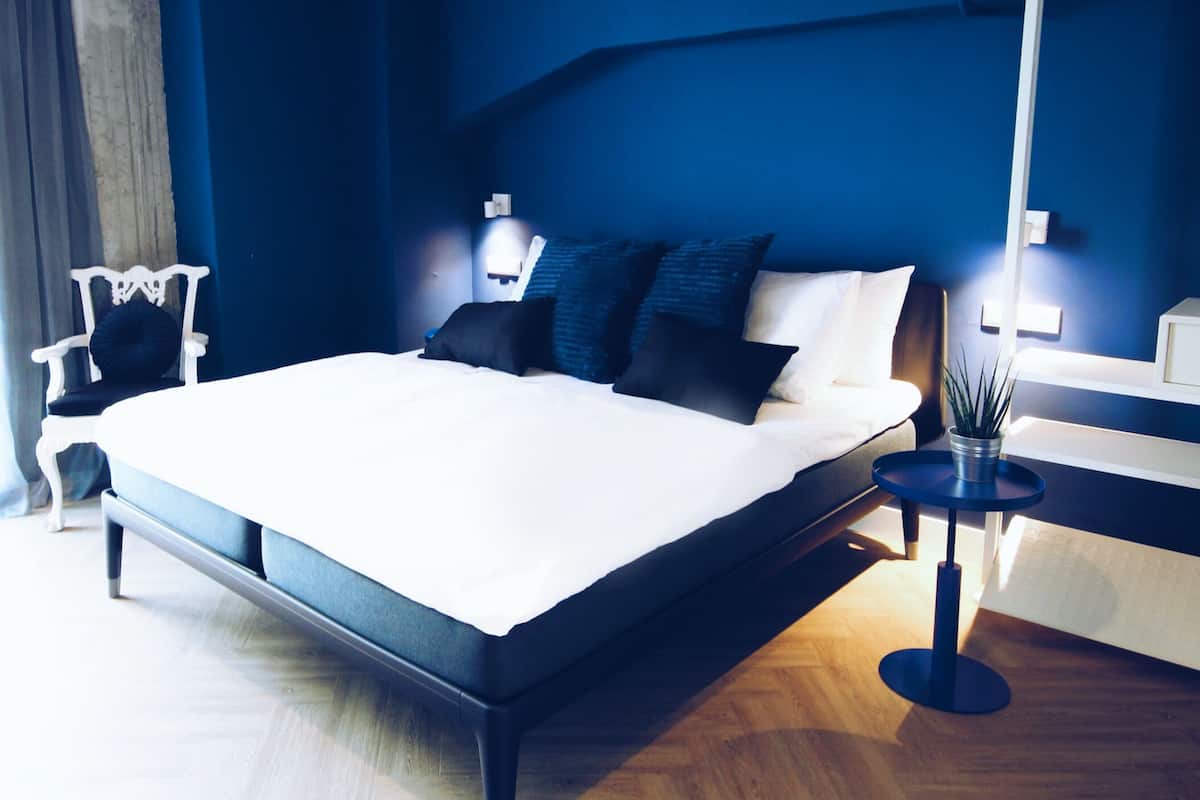 Quarto moderno com uma cama grande, mesas de cabeceira, uma cadeira e um vaso com planta.