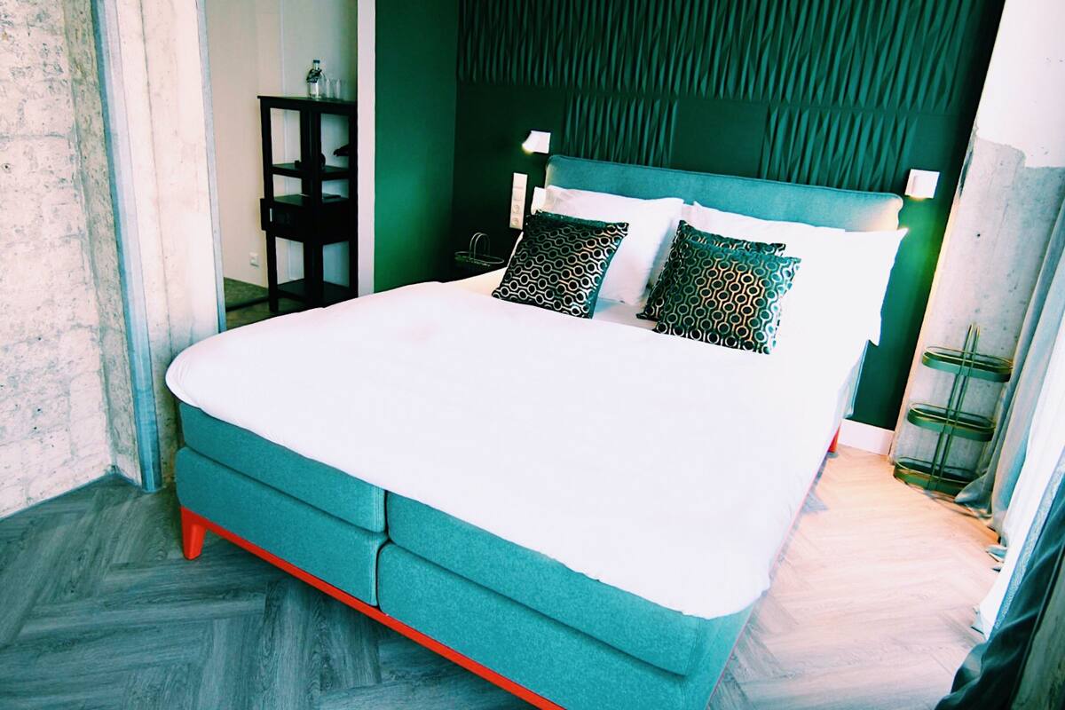 Cama com cabeceira azul-turquesa e pés vermelhos, assoalho de madeira e parede verde-escura.
