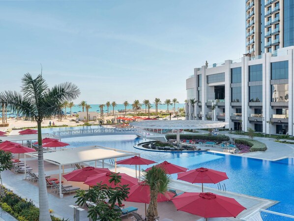 Uma área de piscina em resort com guarda-sóis, espreguiçadeiras e vista para a praia e o oceano.