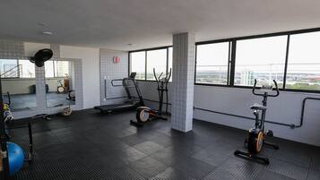 Academia com equipamentos de ginástica, janelas amplas e vista da cidade.