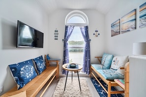 Quarto aconchegante com televisão, sofá, banquinho e vista para a praia.