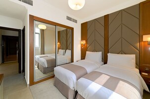 Quarto de hotel com duas camas, um espelho grande e uma cabeceira de madeira.