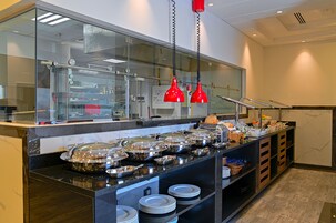 Uma área de buffet com diversas estações de serviço, vitrines de vidro e luminárias pendentes vermelhas.
