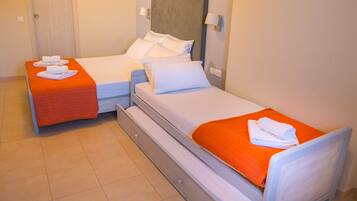 Quarto de hotel com duas camas, cada uma com colcha laranja e roupa de cama branca. Há duas luminárias fixadas na parede, uma de cada lado das camas.