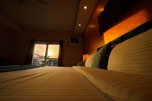Quarto de hotel com cama, vista do pôr do sol pela janela e varanda.