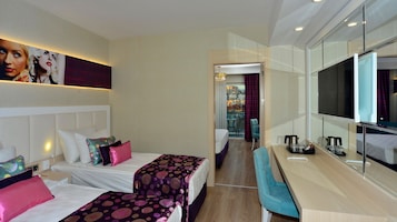Quarto de hotel com duas camas, uma escrivaninha com televisão e vista para a cidade pela janela.