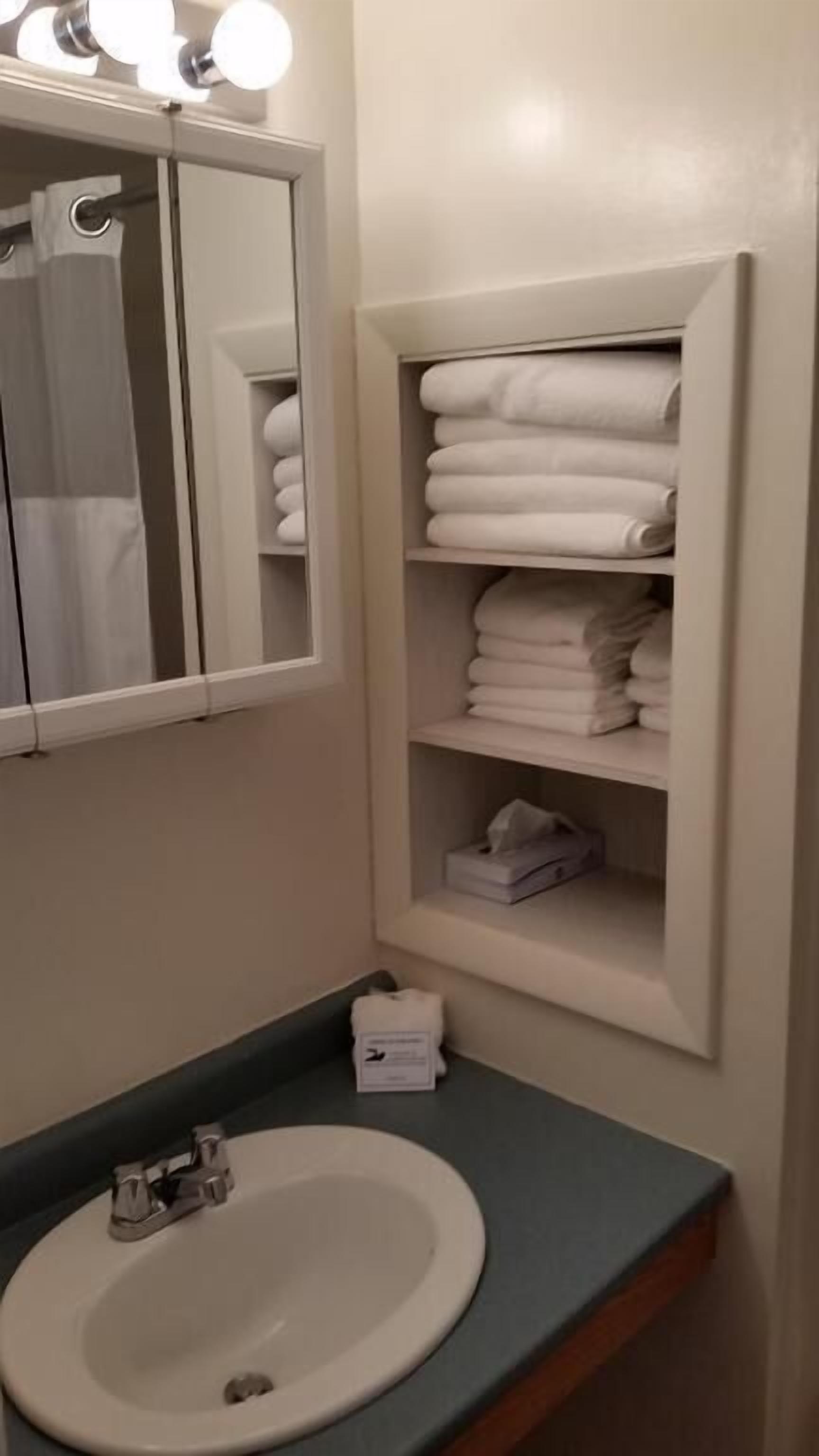 Casa de banho com lavatório, espelho e prateleiras com toalhas dobradas.