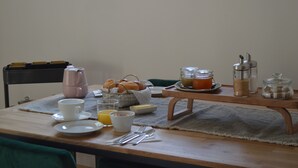 Disposição para o café da manhã com cafeteira, pão, ovos e diversos acompanhamentos sobre uma mesa de madeira.