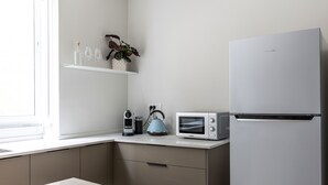 Uma cozinha moderna com uma geladeira branca, um micro-ondas e uma chaleira na bancada. Há uma planta em uma prateleira acima da bancada.