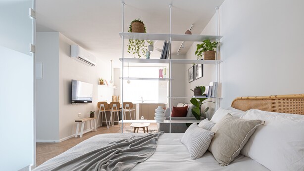 Quarto moderno com cama, televisão, escrivaninha e prateleiras com plantas.