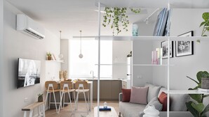 Uma sala de estar moderna com um sofá cinzento, mesa de centro branca e um espaço de jantar com mesa e cadeiras de madeira.