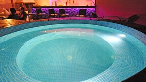 Piscina com borda em azulejo, área de bar com cadeiras e balcão com garrafas.