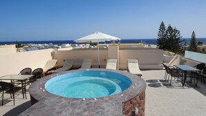 Uma área de piscina no terraço com hidromassagem, espreguiçadeiras e vista para o mar.
