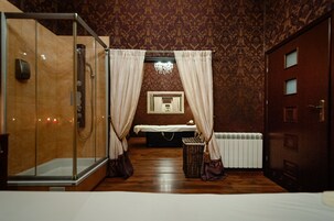 Quarto com chuveiro em cabine de vidro, cama com colcha branca, cômoda e radiador.