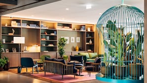Uma área de estar moderna com disposição central de assentos, uma grande estante e uma elegante gaiola azul com plantas.
