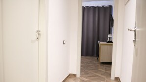 Um corredor estreito com piso ladrilhado que leva a um quarto com uma mesa e uma cadeira.