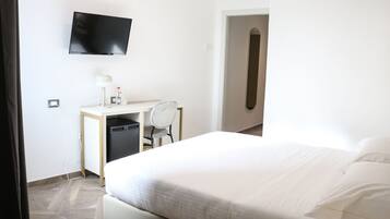 Quarto de hotel com cama, escrivaninha, cadeira, televisão e porta.