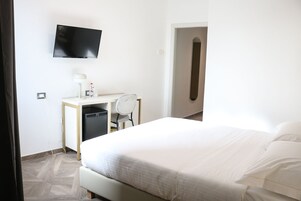 Quarto de hotel com cama, escrivaninha, cadeira, televisão e porta.