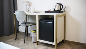 Quarto de hotel compacto com escrivaninha, cadeira e um pequeno frigorífico.