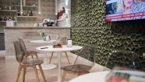 Interior moderno com mesas redondas, cadeiras transparentes e uma televisão fixada numa parede texturizada.
