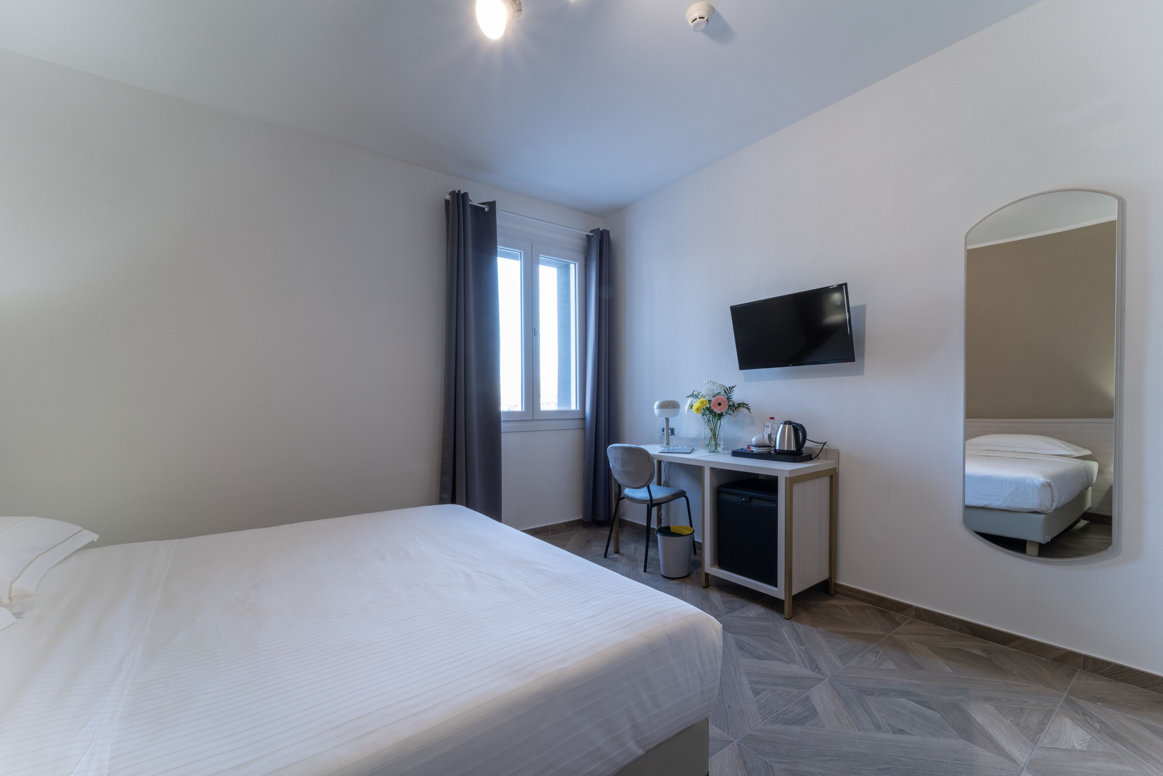 Quarto de hotel com cama, secretária com cadeira, televisão e espelho.