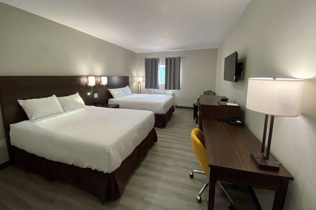 Quarto de hotel com duas camas, uma escrivaninha, uma cadeira, uma televisão e uma janela com cortinas.