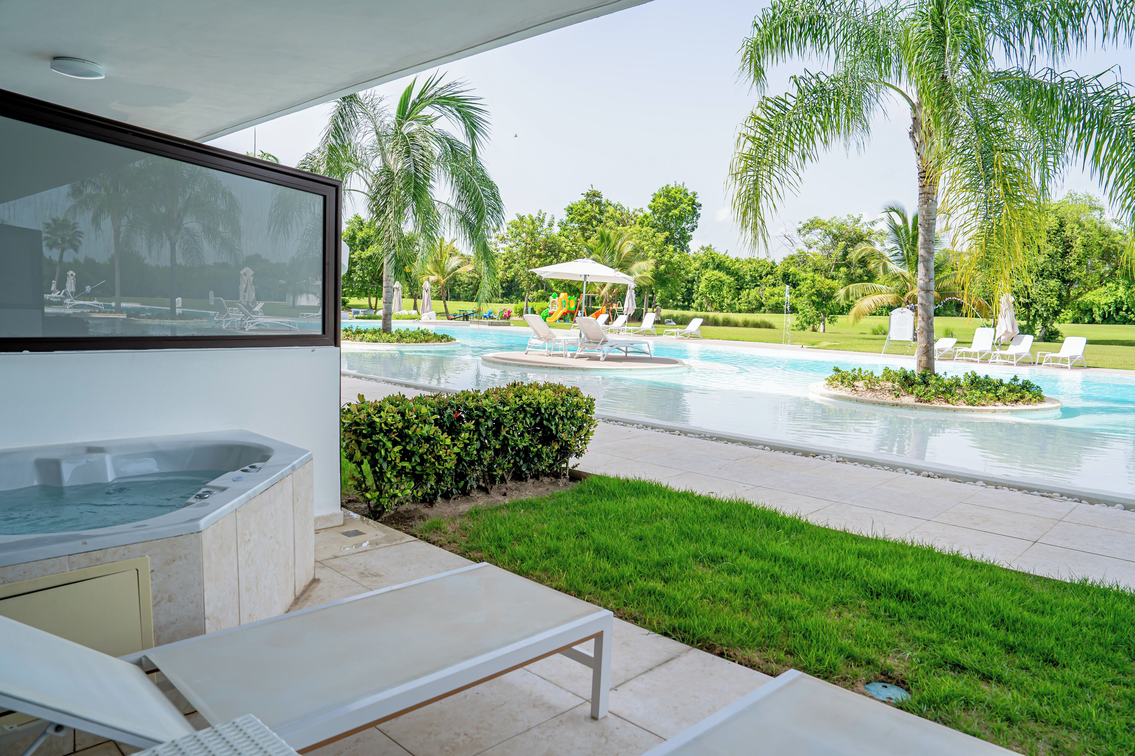 Uma área de piscina moderna ao ar livre, com espreguiçadeiras, hidromassagem e vista para um toboágua e vegetação.