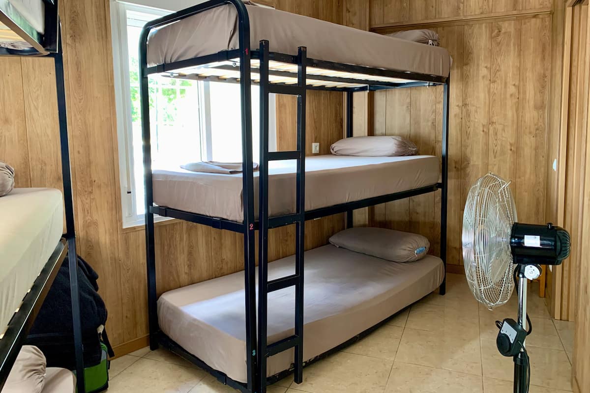 Quarto com beliche, janela e uma mala verde no chão.