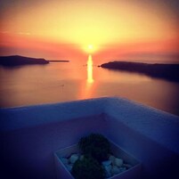 Vista do pôr do sol vista de uma varanda com um cachepot de pedras e plantas.