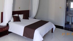 Cama bem arrumada com roupa de cama branca e marrom, cabeceira de madeira e mesa de cabeceira com gaveta.